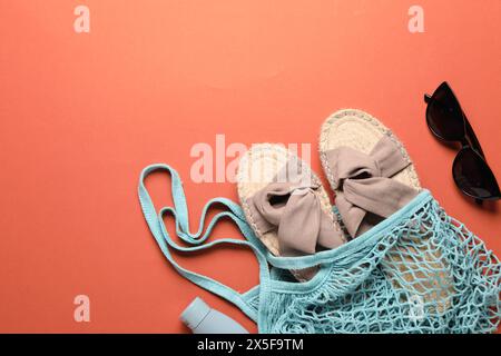 String bag, sunglasses, cosmetic product and slippers on coral ...