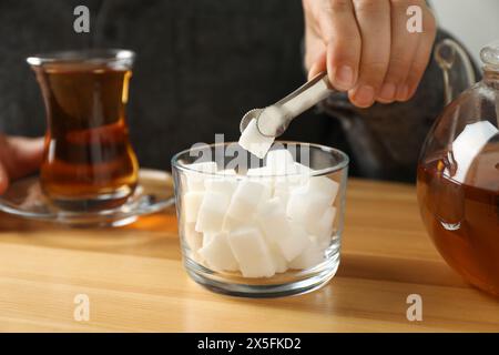 Woman adding sugar cube into aromatic tea at wooden table, closeup ...