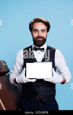 Classy bellhop presenting tablet on camera and showing isolated white ...