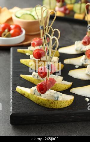 Tasty canapes with pears, blue cheese and prosciutto on grey table ...