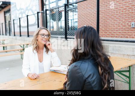 Two women talking, laughingm and wording at a table outside Stock Photo ...