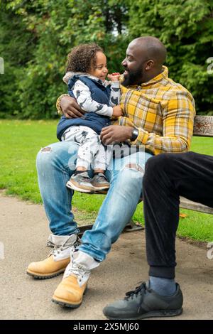 Father and daughter sitting on bench with hands together at street ...