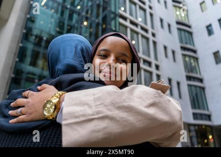 Two women wearing hijabs hugging in street Stock Photo - Alamy
