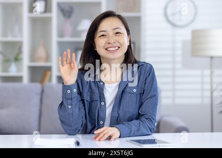 Asian woman waving during video call on laptop computer smiling happy ...