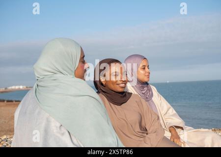 Three Muslim friends sitting on beach Stock Photo - Alamy