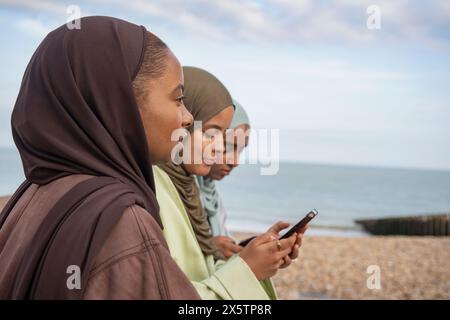 Three Muslin women using smart phones while sitting by sea Stock Photo ...