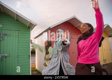 Cheerful Muslim friends waving while walking next to beach huts Stock ...