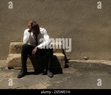 Worried black man sitting on floor in street having problems rubbing ...