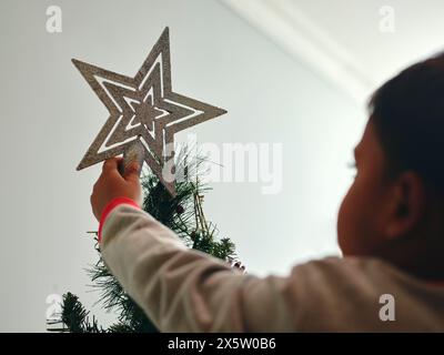 the boy has a star on the top of the Christmas tree in his hands Stock ...