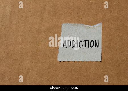 Addiction word written on ripped blue paper piece with brown background ...