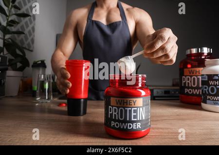 Handsome muscular man making protein shake with powder in kitchen ...