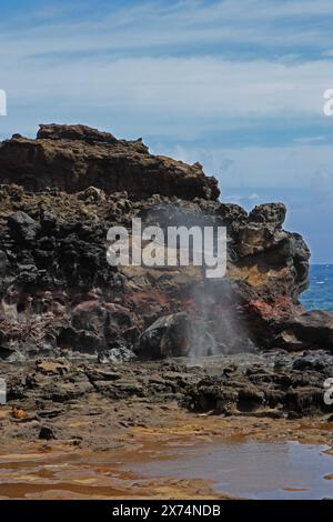 Mist rising from the Nakalele Blowhole surrounded by volcanic rock and ...