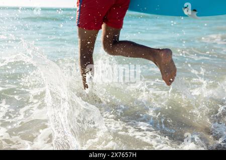 At beach, young biracial man running into sea holding surfboard Stock ...