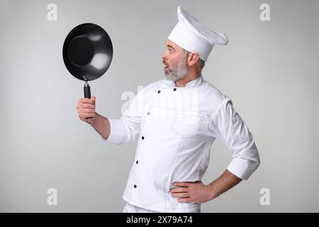 Surprised chef in uniform holding wok on grey background Stock Photo ...