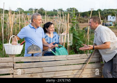 Three neighbours farmers talking together near wooden fence in garden ...