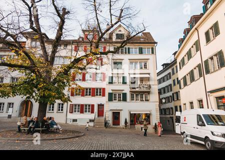People sit beneath a large deciduous tree in a Zurich city square in ...
