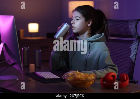 Girl with energy drink playing computer game at table in room Stock ...
