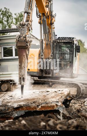 Excavator breaks up concrete and rubble and dust can be seen on a ...