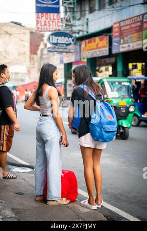 Two young filipino girlfriends wait for a bus or jeepney in the Tondo ...