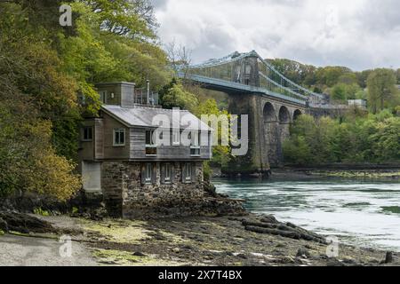 House on the banks of the Menai Strait with Menai suspension bridge in ...
