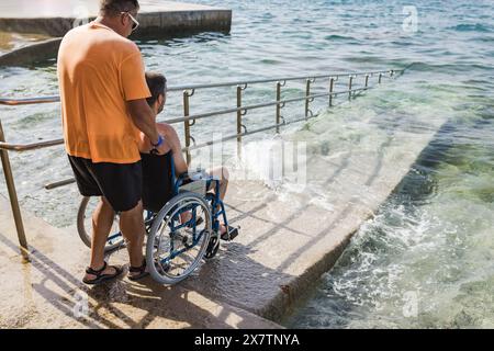Wheelchair user entering the sea with the help of an assistant on ...