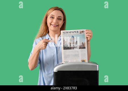 Adult woman pointing at newspaper and shredder on green background ...