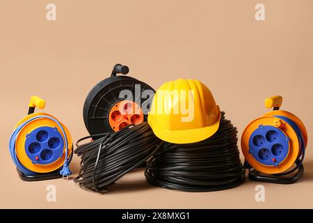 Rolled wires, hardhat and extension cable reels on beige background ...