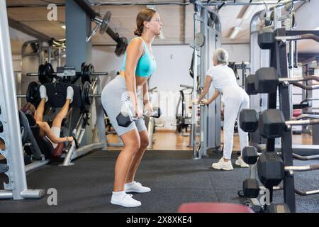 Slender girl trains muscles of arms and back using barbell and ...