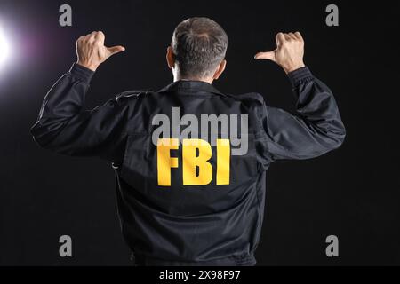 Mature FBI agent pointing at himself on black background, back view ...