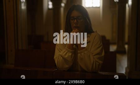 A young hispanic woman prays in a christian church in italy, surrounded ...