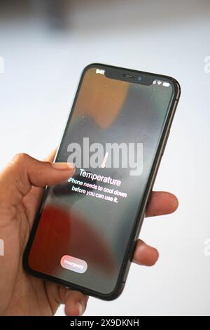 A hand holding a smartphone displaying a temperature warning message ...