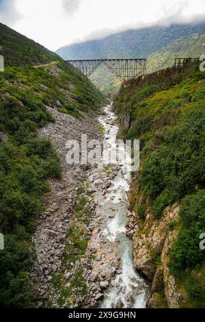 A historic railroad bridge in the Alaskan mountains stands partially ...