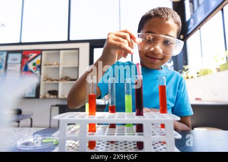 Biracial boy conducts an experiment in a science classroom at school ...