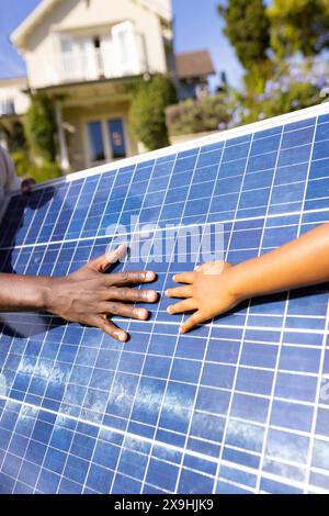 Outdoors, diverse father and daughter touching solar panel together ...