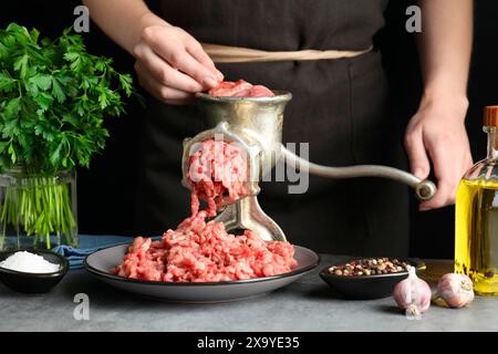Woman making beef mince with manual meat grinder at table against black ...