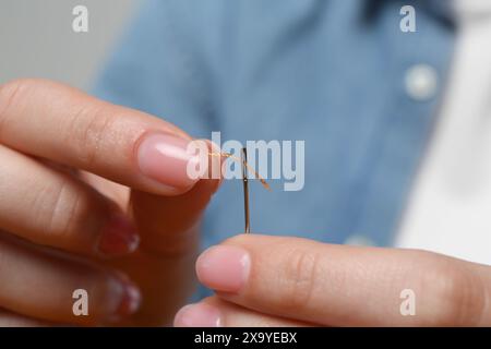 Woman inserting thread through eye of needle on blurred background ...
