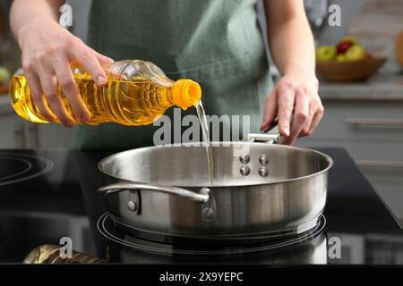 Vegetable fats. Woman pouring oil into frying pan on stove, closeup ...