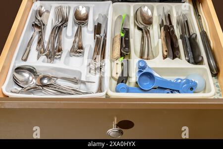 Horizontal shot of a messy and cluttered silverware drawer in the home ...