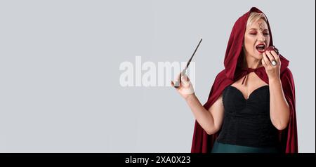 Mature witch with magic wand eating apple on grey background Stock ...