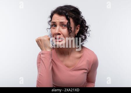 Portrait of a crying curly woman with a short haircut in a pink blouse ...