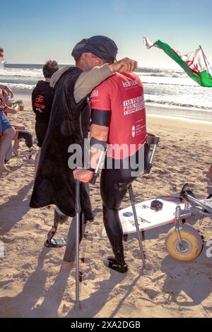 A parasurfer amputee uses crutches while a companion carries his ...