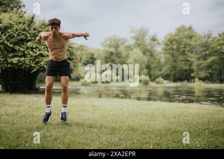 Flexible man performing back flip in a park near a lake on a summer day ...