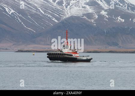 Tug boat in Faxi's Bay, Reykjavik, with snow covered mountains in the ...