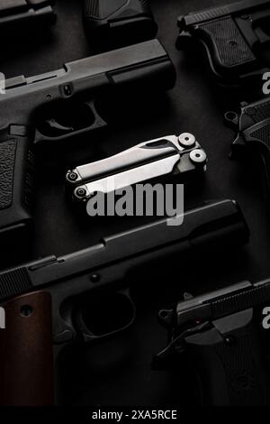 Silver multi-tool among various semi-automatic pistols. Dark background ...