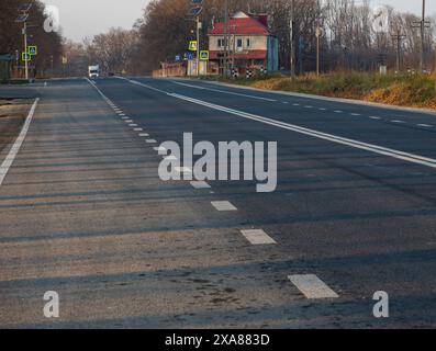 Road lined with autumn trees. Cross hatching road marks line the centre ...