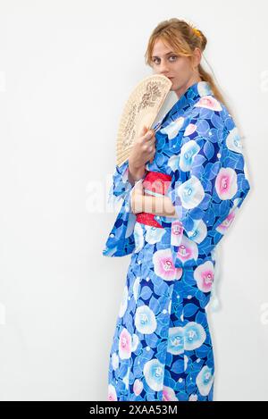 A female cosplayer in a blue kimono with a red sash holding a wooden ...