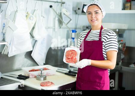 Female butcher demonstrating freshly formed beef hamburger patties ...