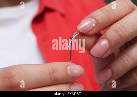 Woman inserting thread through eye of needle on blurred background ...