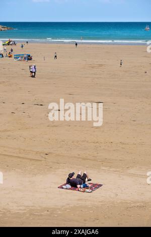 A mature male holidaymaker lying down alone on a blanket on a beach in ...