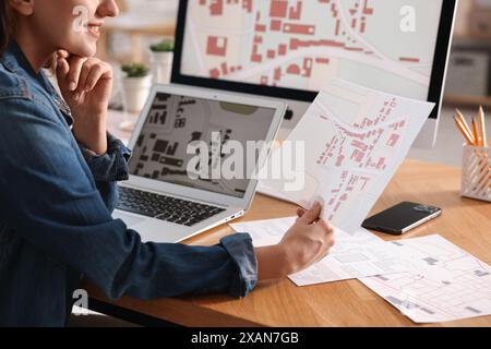 Smiling cartographer working with cadastral maps at table in office ...